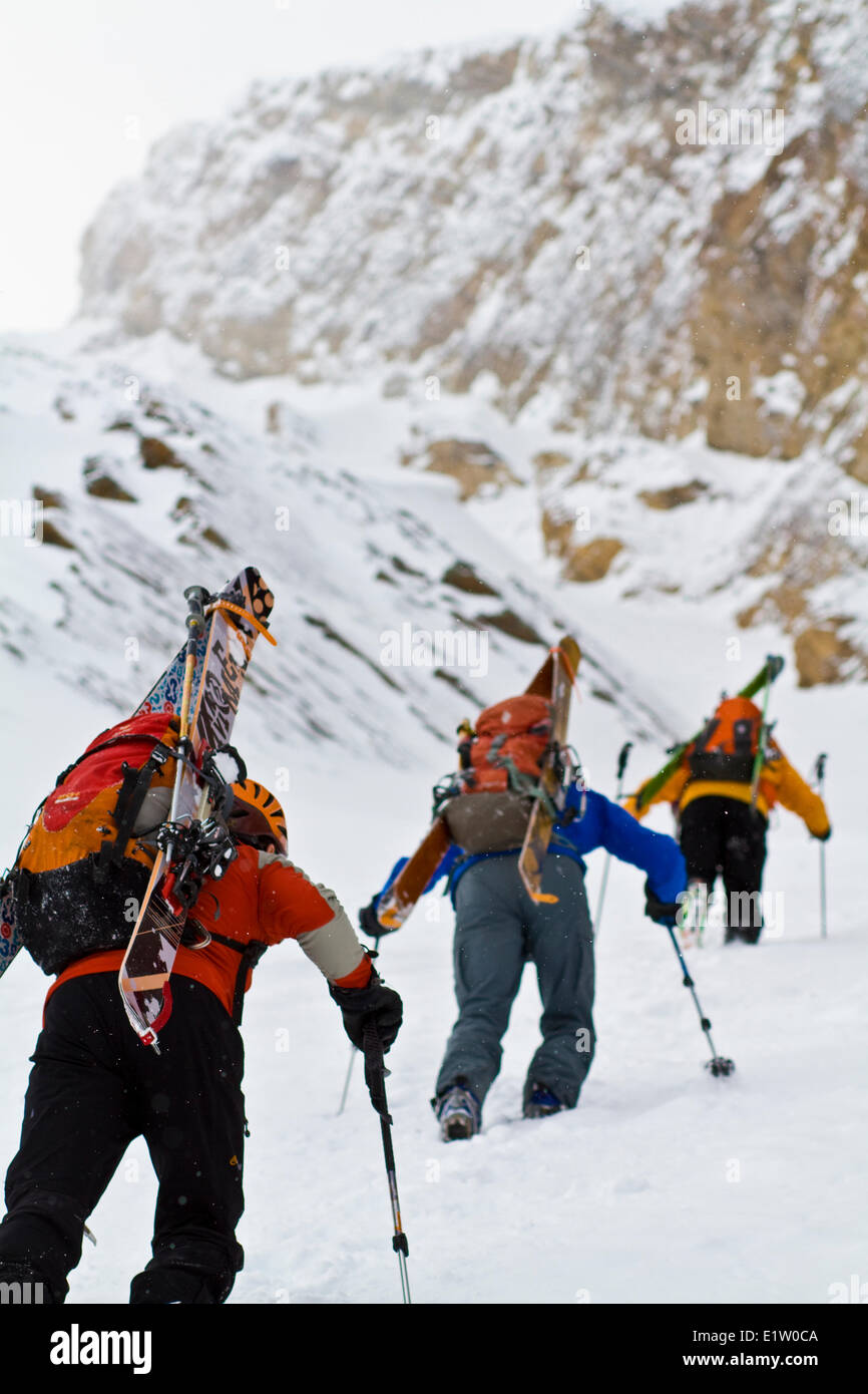 Three male backcountry skiers bootpack up a steep and committing line ...
