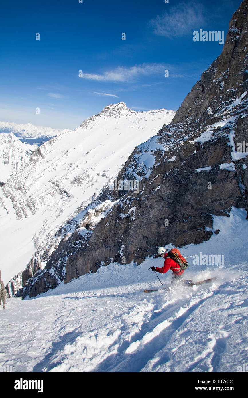 A male backcountry skier on tele skis descends a steep couloir with a ...