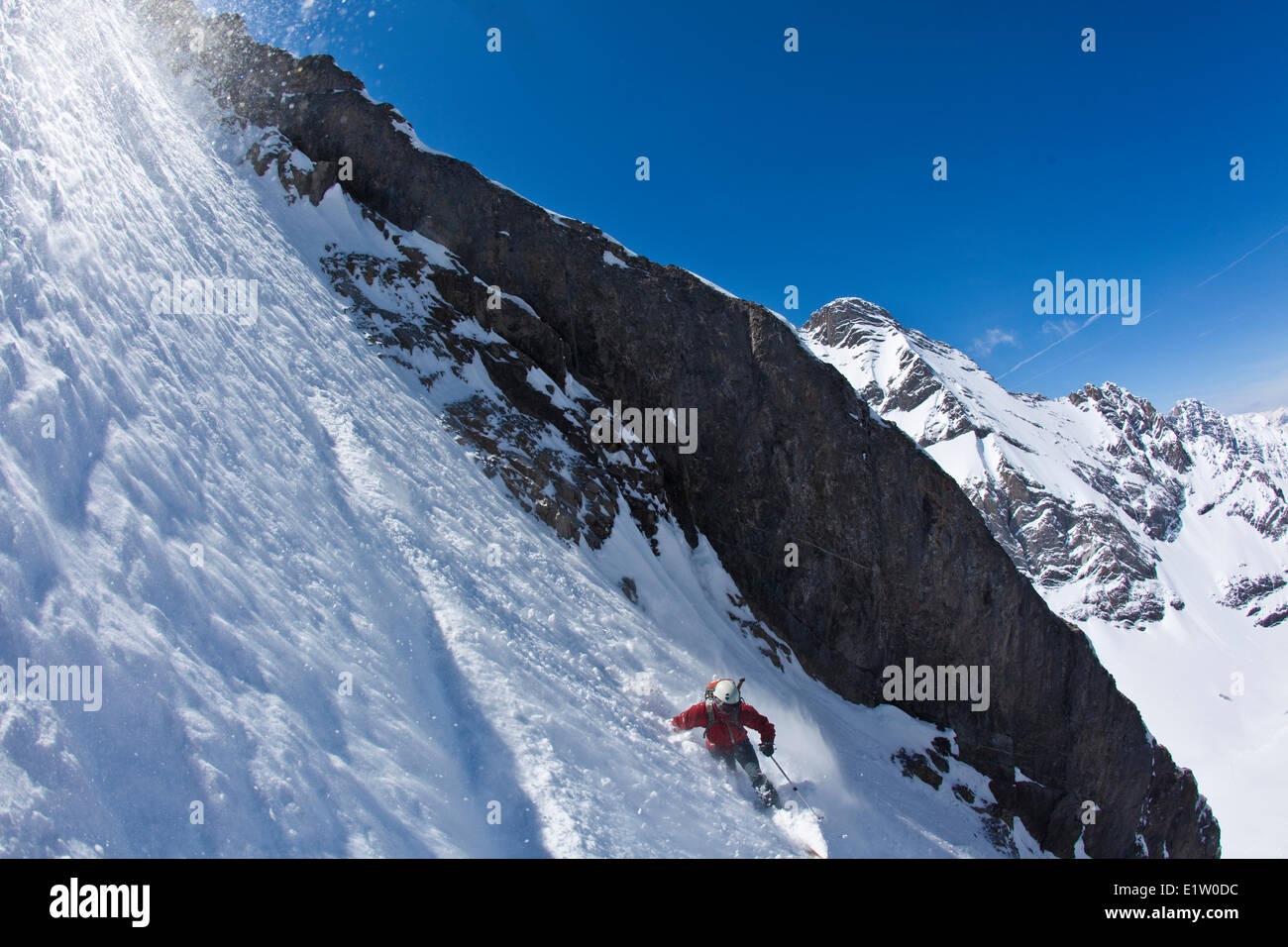 A male backcountry skier on tele skis descends a steep couloir with a ...