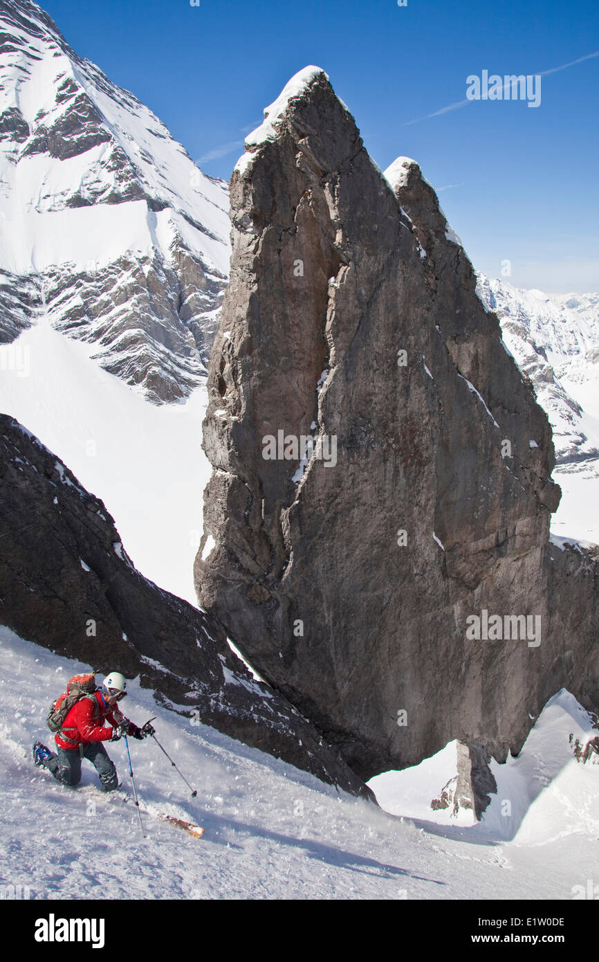 A male backcountry skier on tele skis drops into a steep couloir with a ...