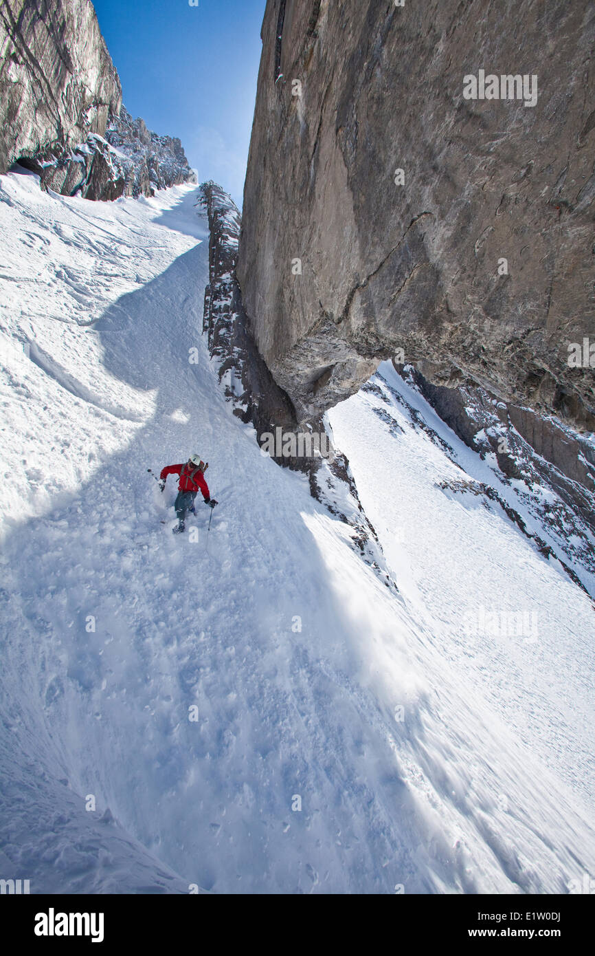 A male backcountry skier on tele skis drops into a steep couloir with a ...