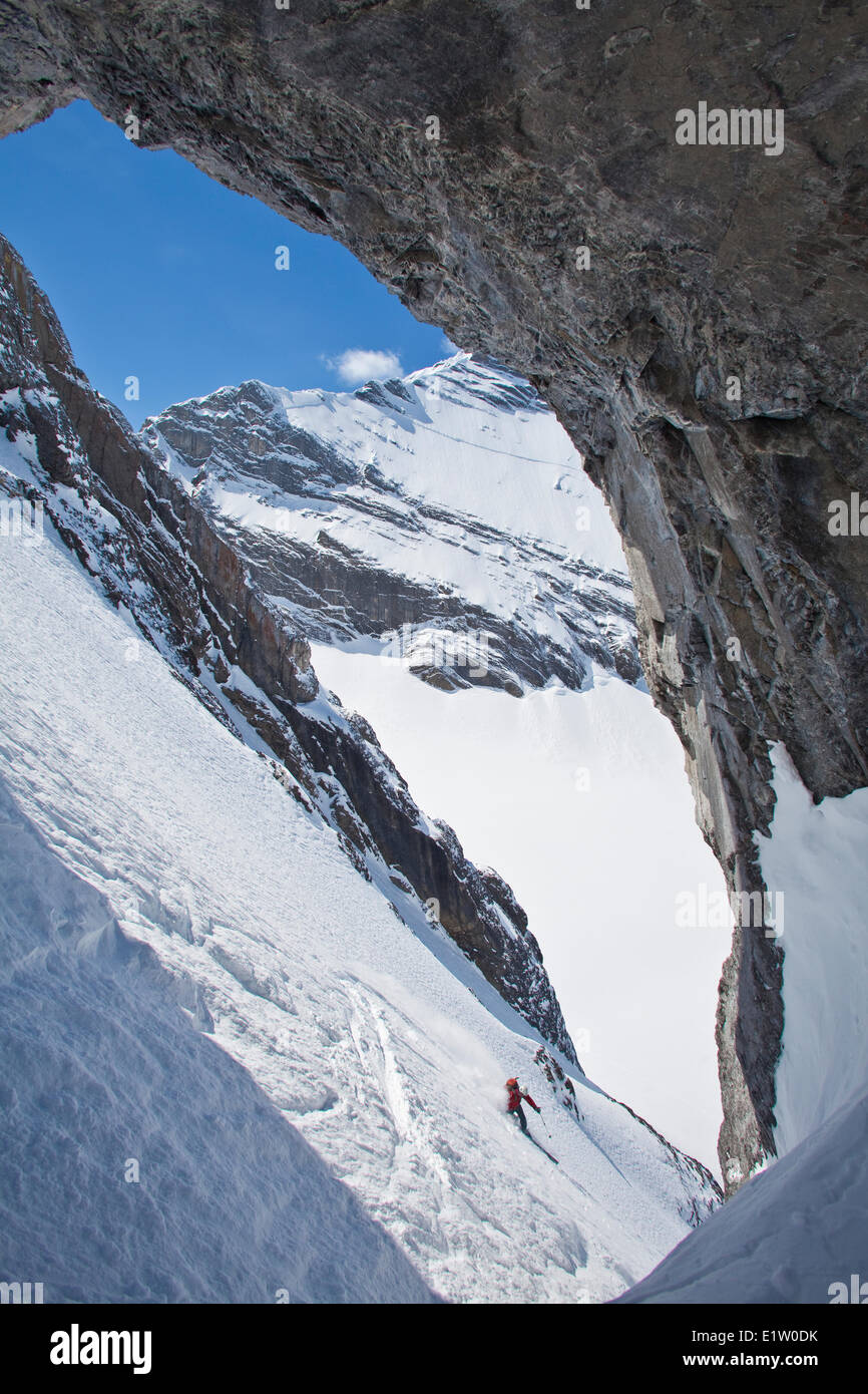 A male backcountry skier on tele skis drops into a steep couloir with a ...