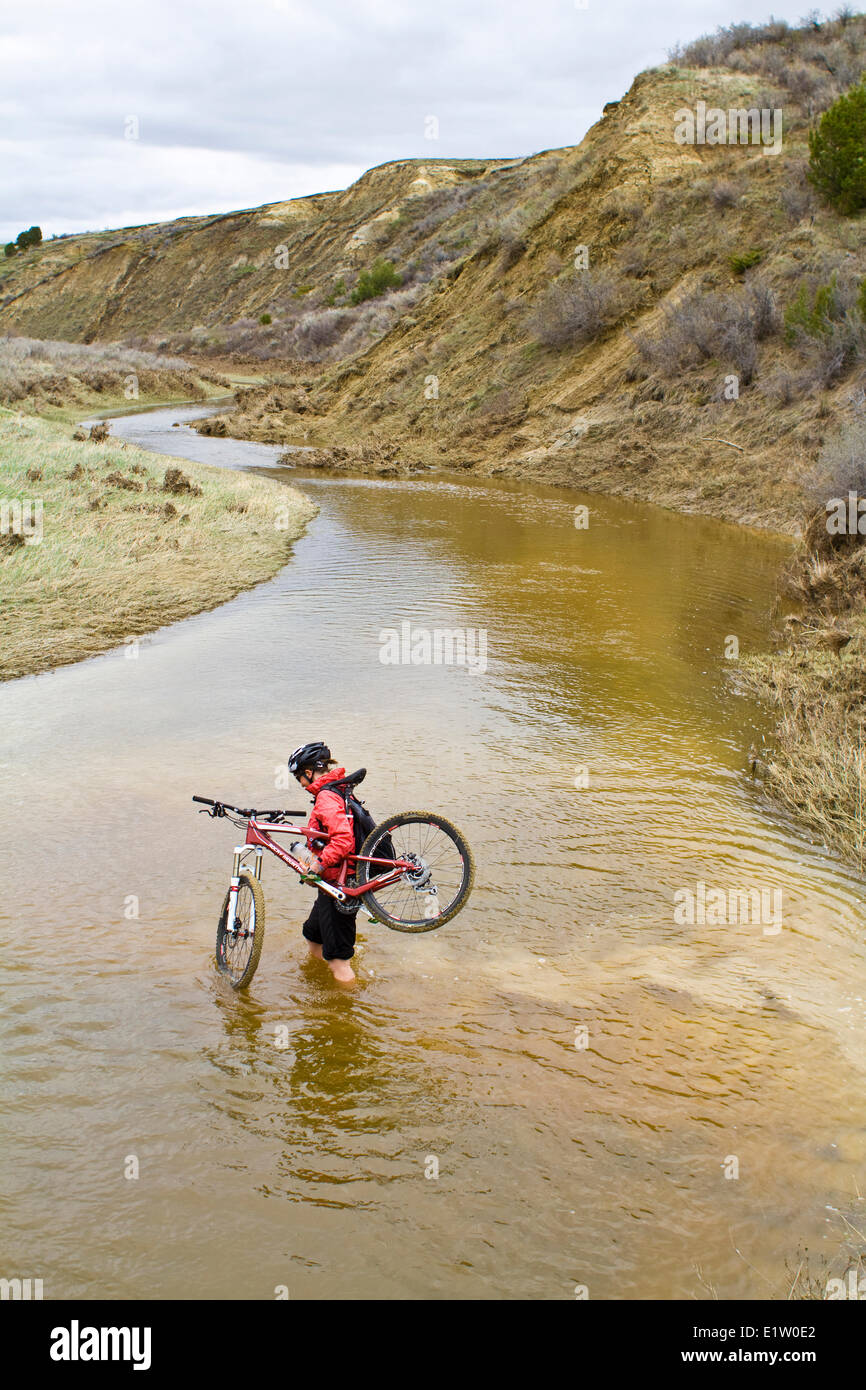 A woman walks her mountain bike through spring run off conditions on ...