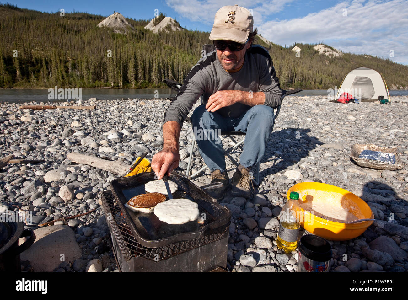 MIddle-aged man cooking pancakes over firebox while camped on Nahanni ...