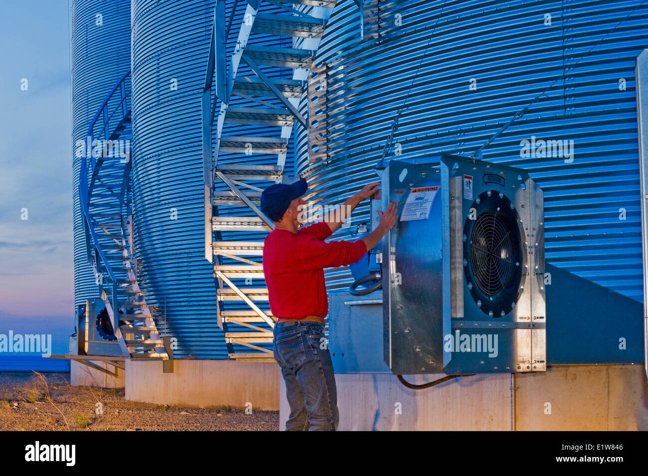 Man turns on an aeration fan on a grain storage bin in the evening ...