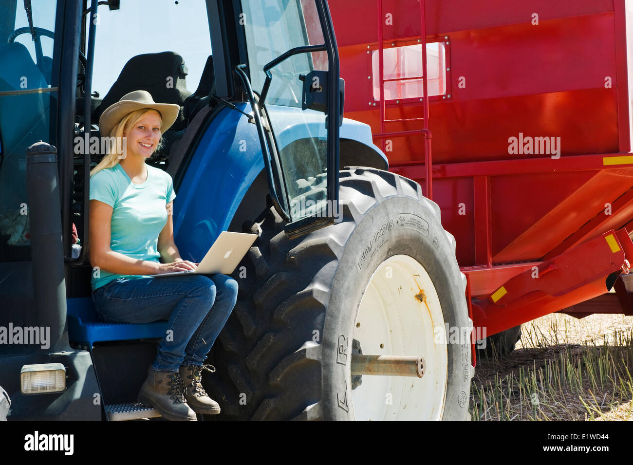 a farm girl uses a laptop computer on the deck of a tractor with grain ...