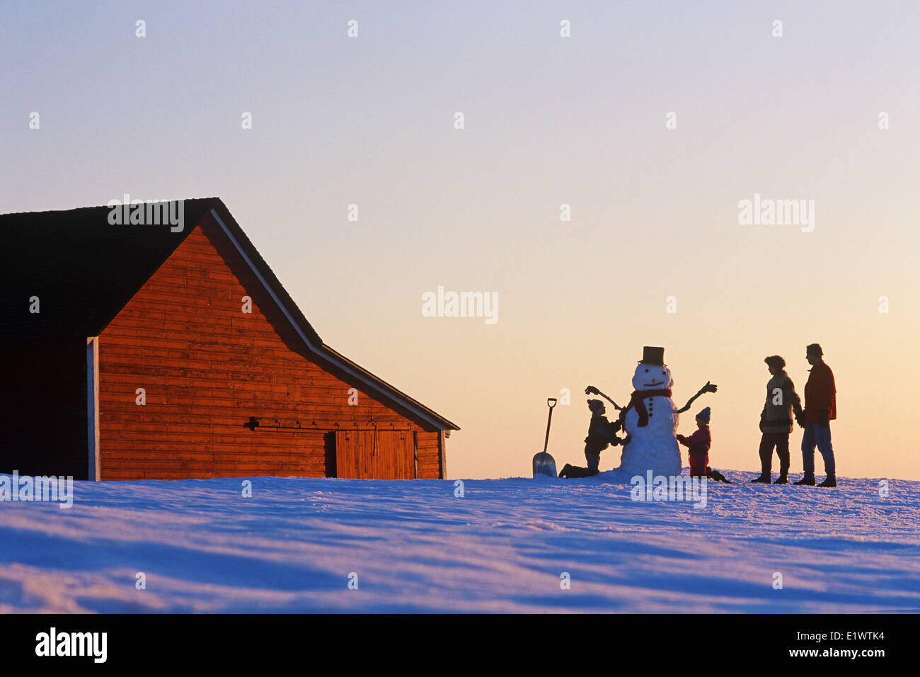 a family make a snowman in front of a red barn, near Glass, Manitoba ...