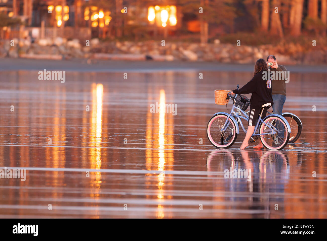 A couple photographs each other at sunset while riding beach cruisers ...