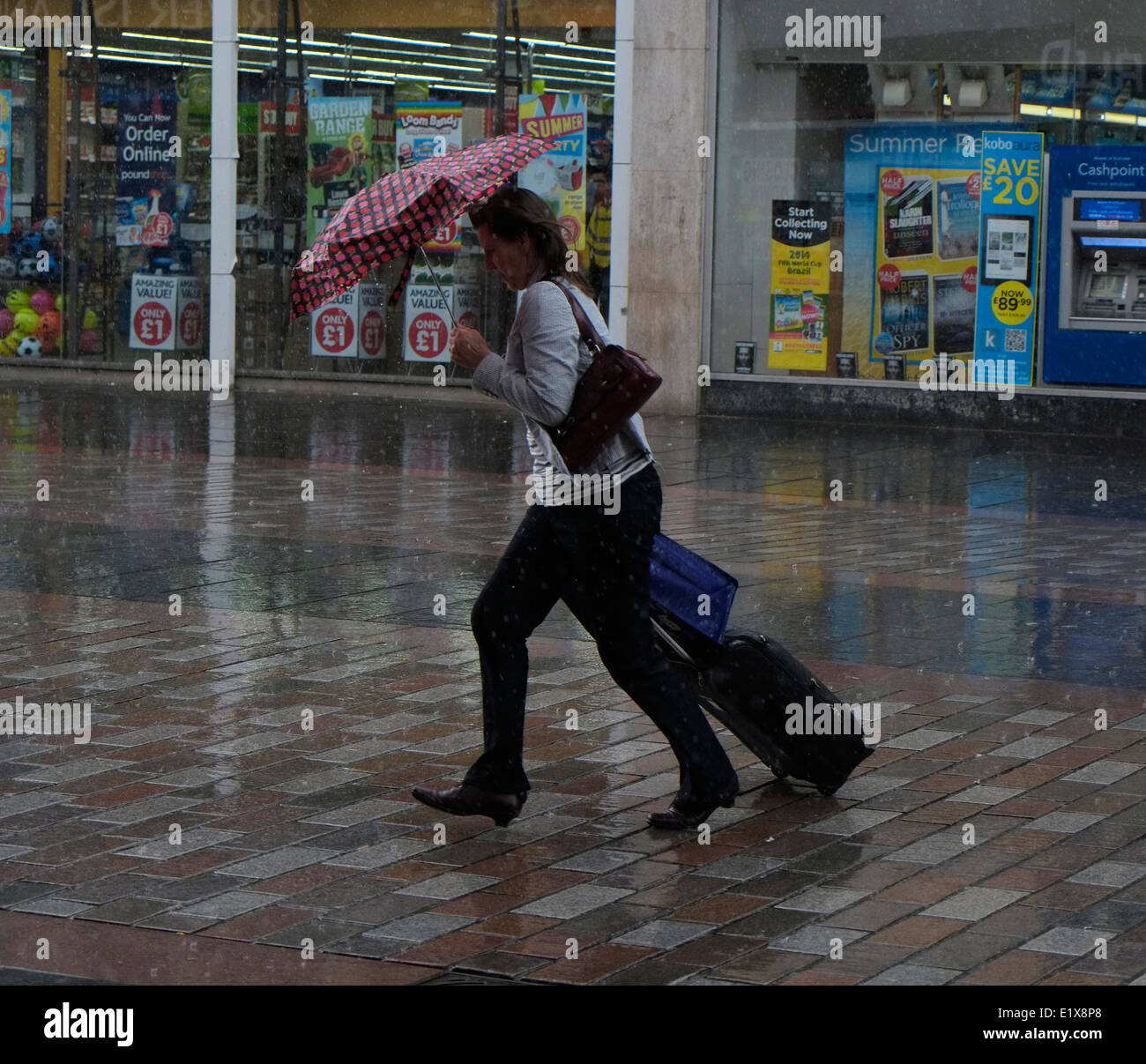 Woman walking along a street in the rain pulling a bag on wheels Stock ...