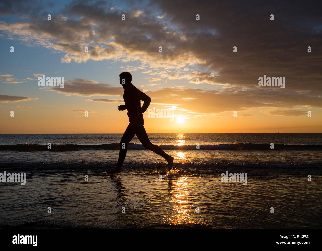 Jogger running barefoot in the sea at sunrise. UK Stock Photo - Alamy
