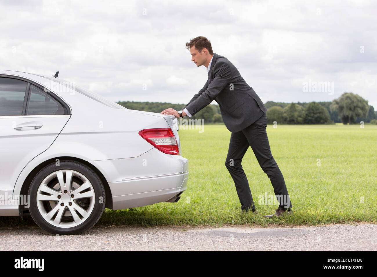 Full length side view of young businessman pushing broken down car at ...