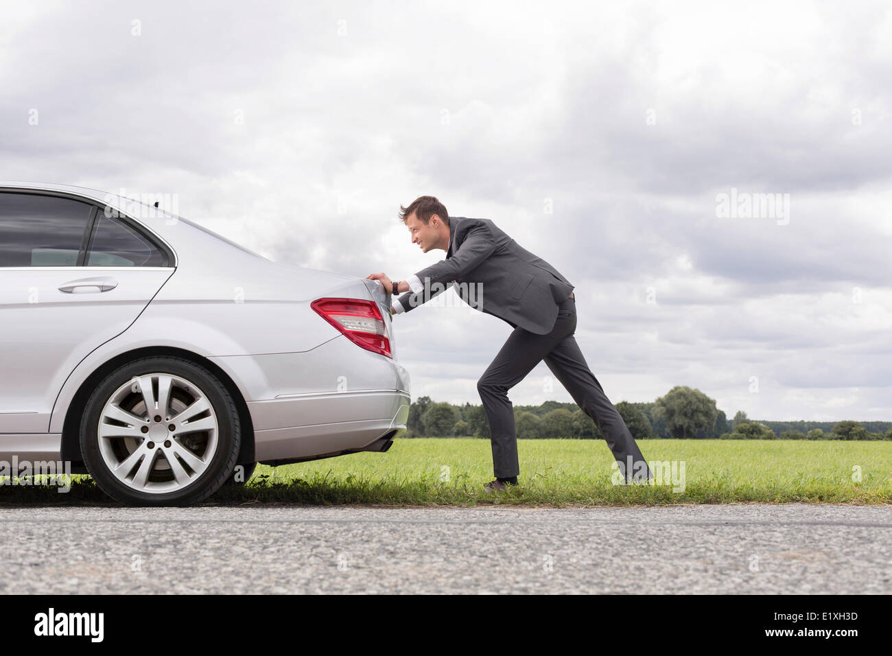 Full length side view of young businessman pushing broken down car on ...