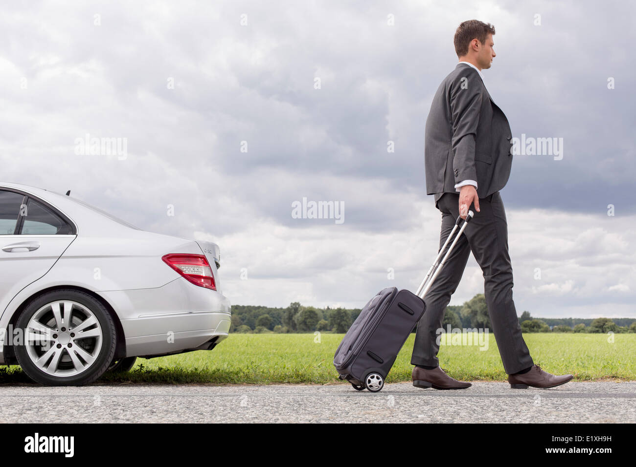 Full length side view of young businessman with luggage leaving broken ...