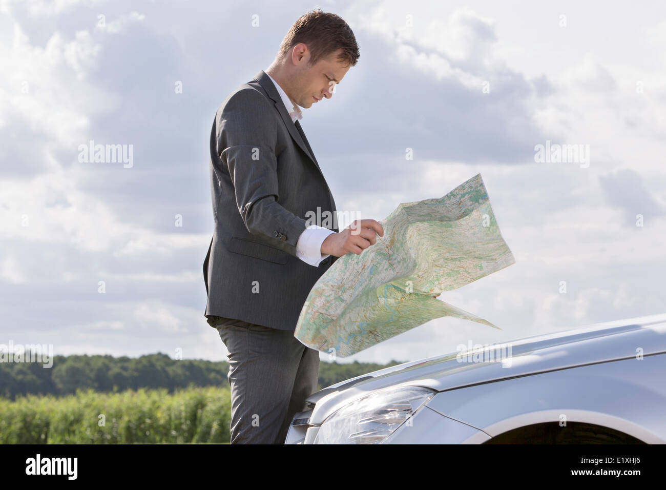 Side view of young businessman reading map by car at countryside Stock ...