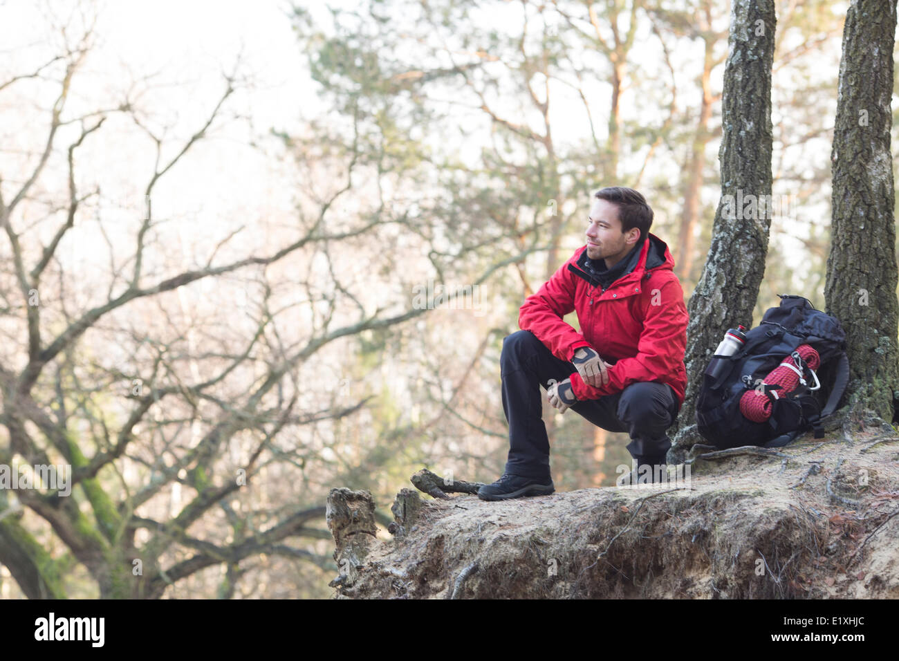 Full length of male hiker crouching on cliff in forest Stock Photo - Alamy