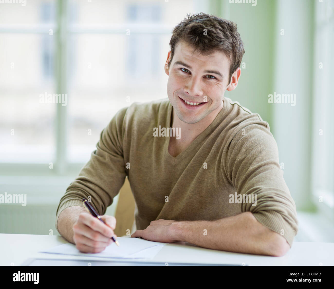 Portrait of handsome businessman writing on document at desk in office ...