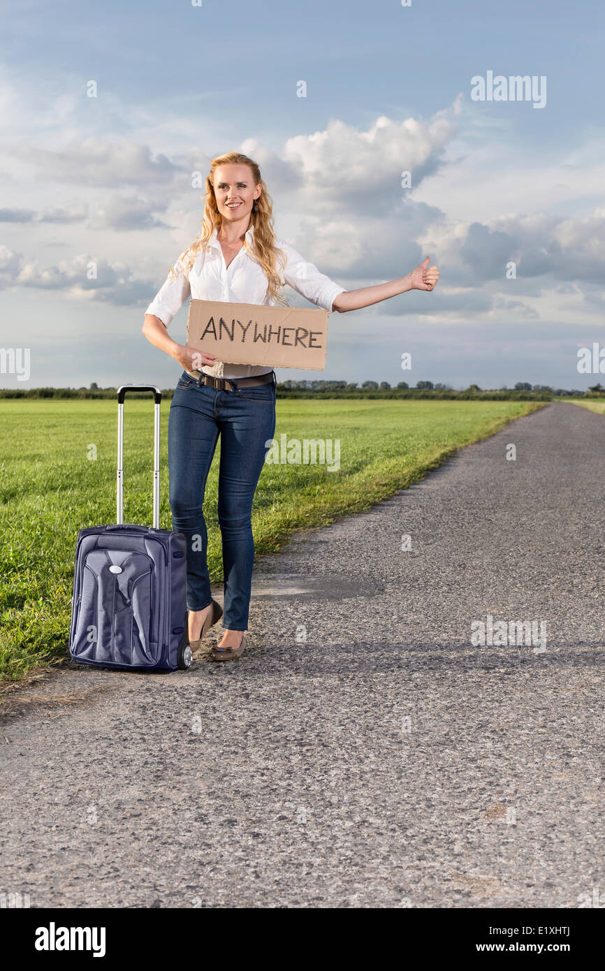 Full length of woman hitching while holding anywhere sign on ...
