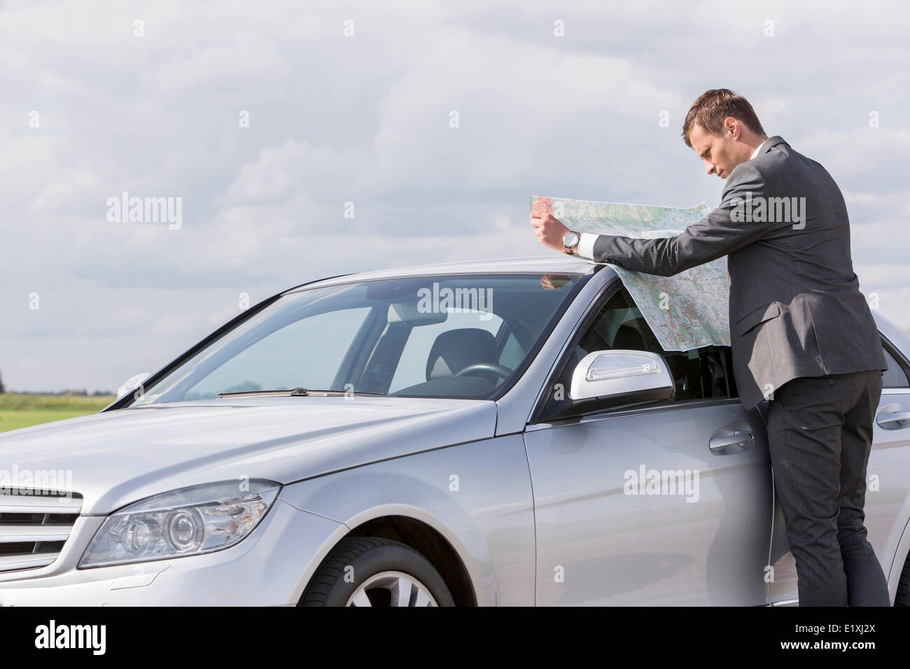 Side view of young businessman reading map by car at countryside Stock ...