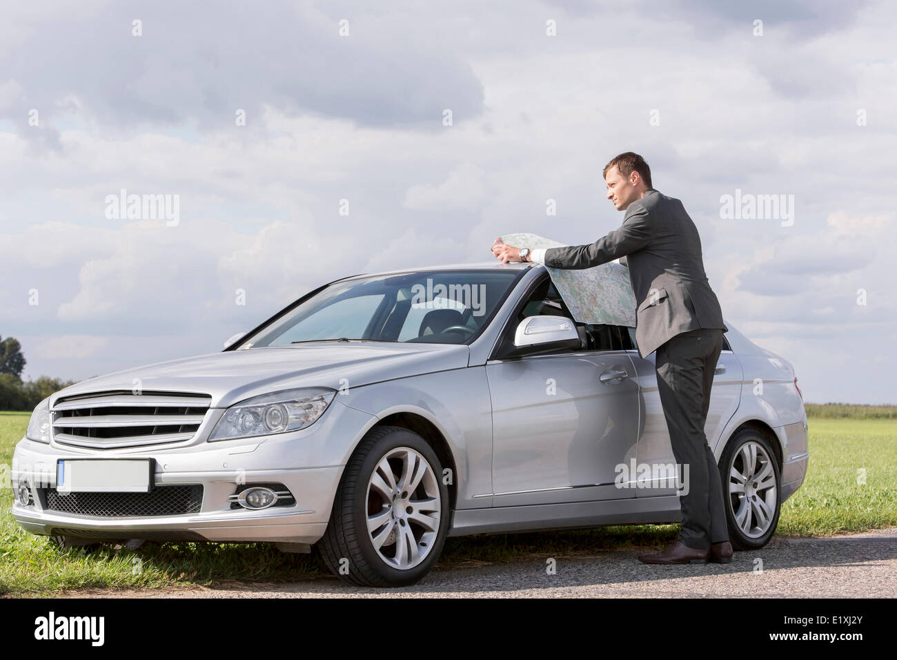 Full length of young businessman reading map by car at countryside ...