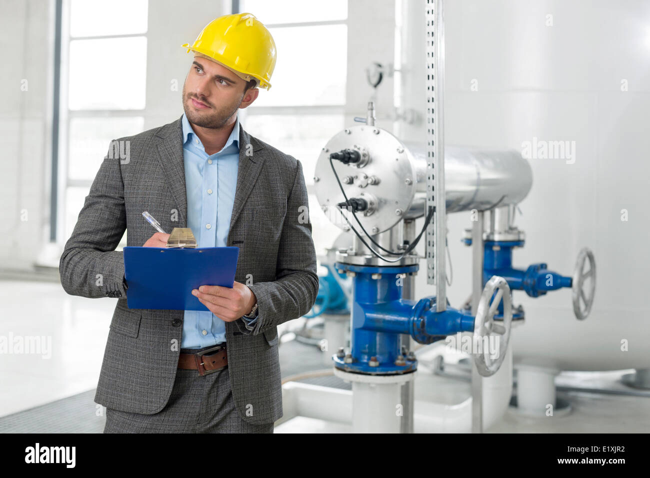 Young male inspector writing on clipboard while looking away in ...