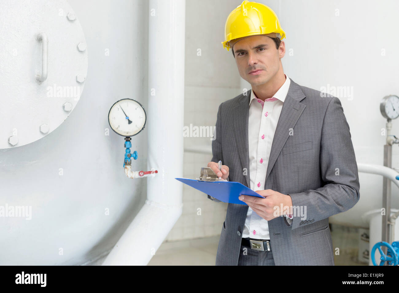 Portrait of confident young male inspector writing on clipboard in ...