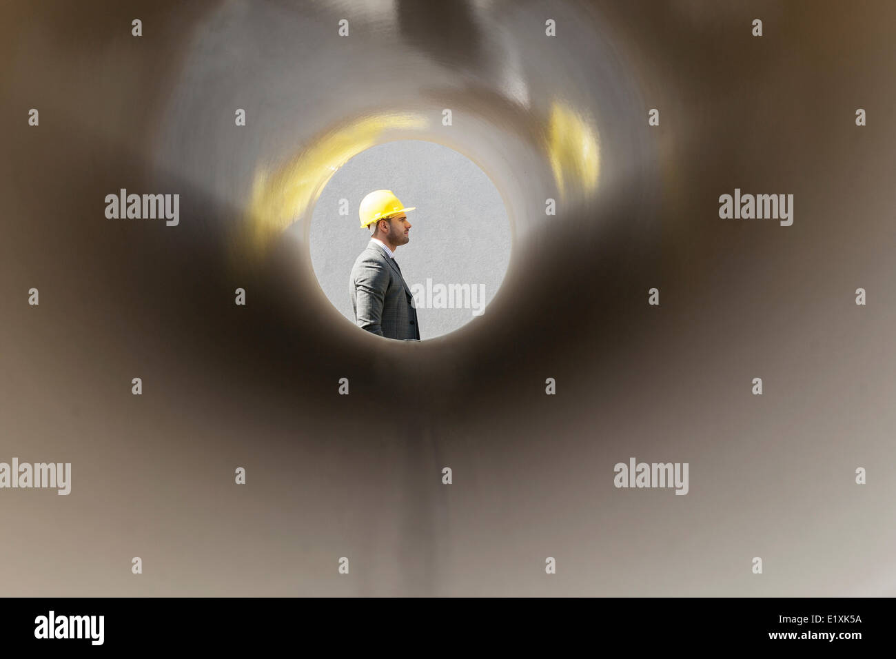 Side view of young male architect through large pipe at construction ...