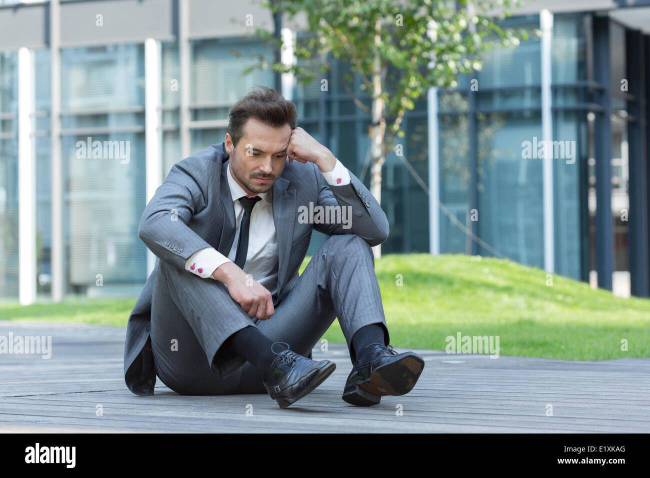 Full length of depressed businessman sitting on path outside office ...
