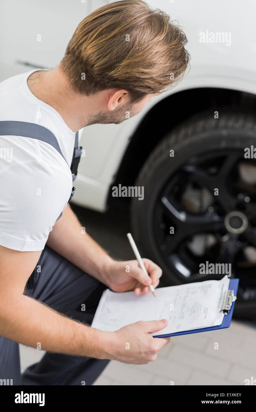 Side view of automobile mechanic writing on clipboard while examining ...