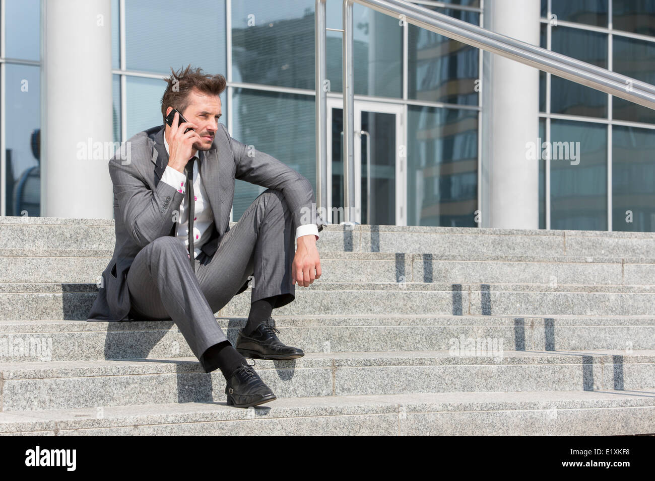 Full length of young businessman answering cell phone on steps outside ...