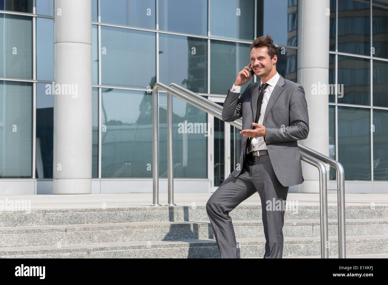 Smiling businessman using cell phone while standing on steps outside ...