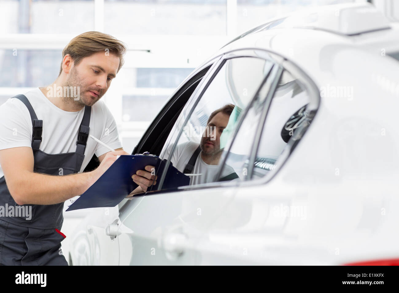 Automobile mechanic writing on clipboard while examining car in repair ...