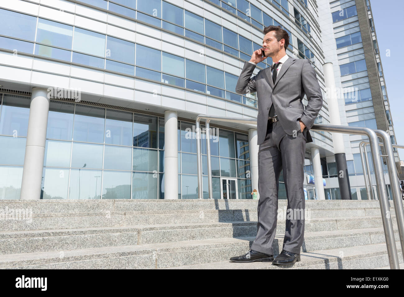 Full length businessman answering cell phone while standing on steps ...