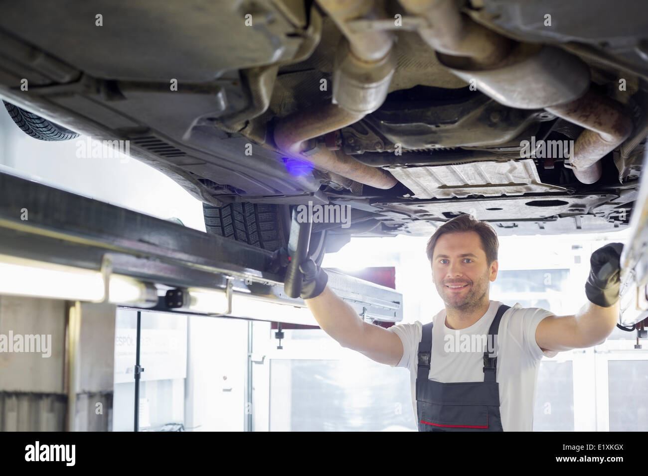Portrait of smiling repair worker examining car in workshop Stock Photo ...