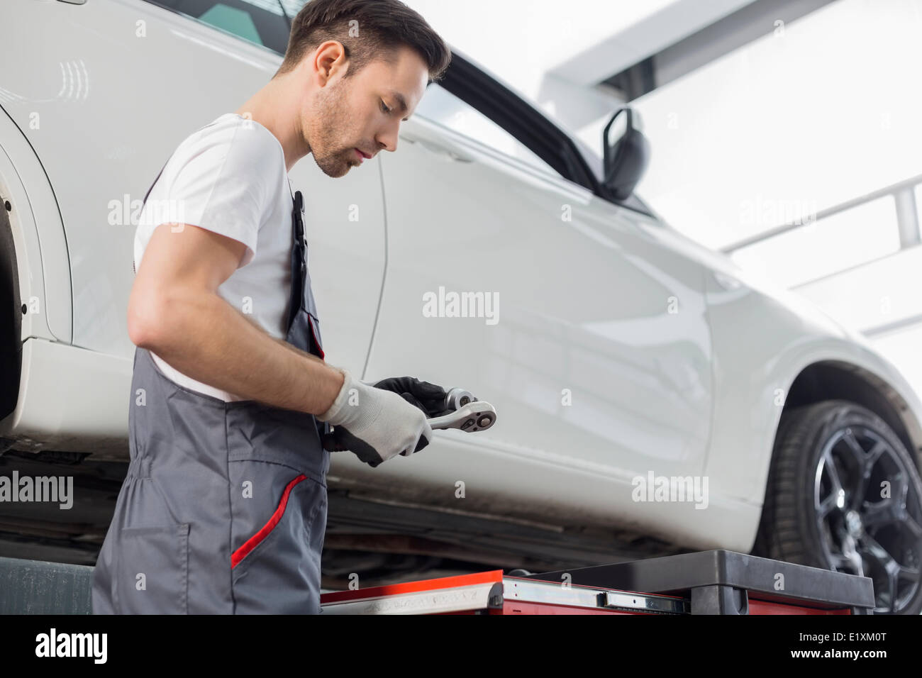 Side view of repairman holding tool while standing by car in workshop ...