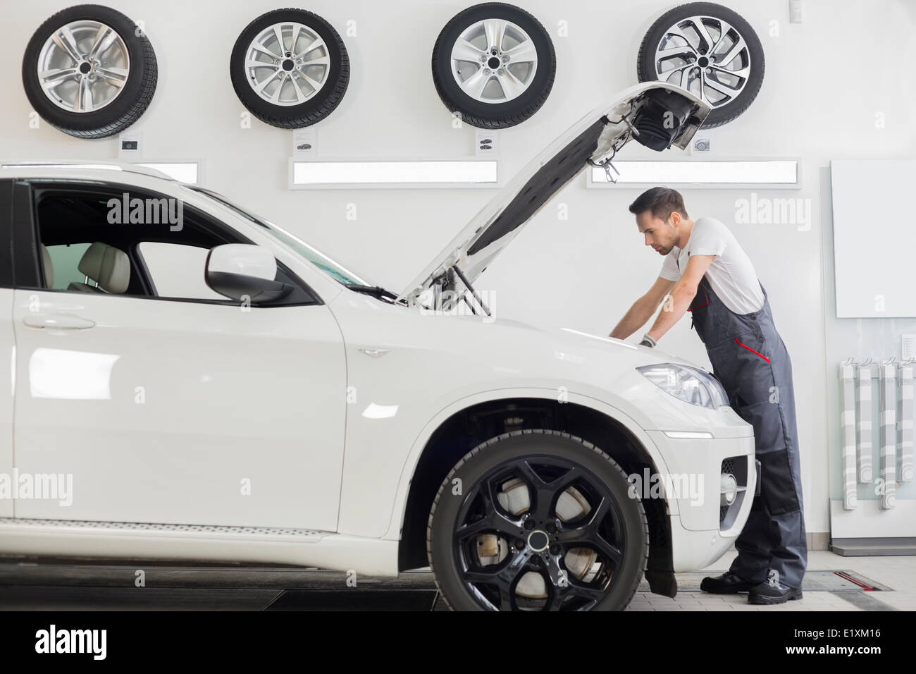 Full length side view of male mechanic examining car engine in repair ...
