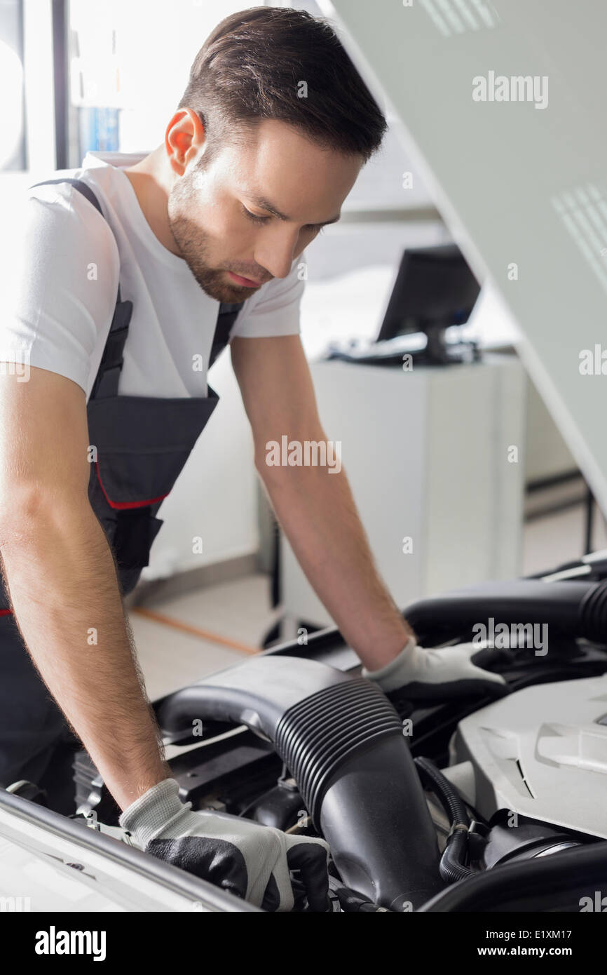 Full length side view of male mechanic examining car engine in repair ...