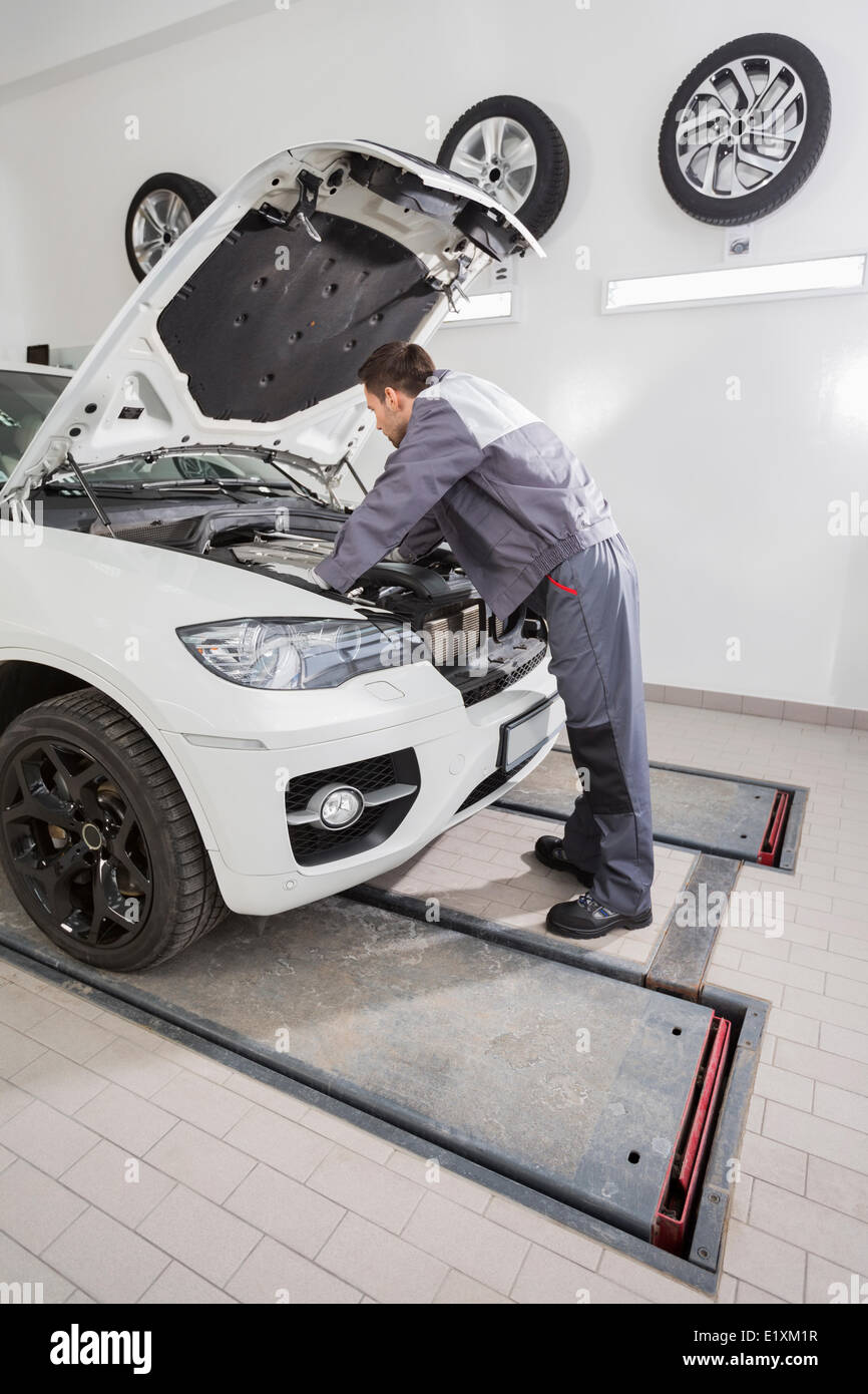 Full length side view of male automobile mechanic repairing car engine ...