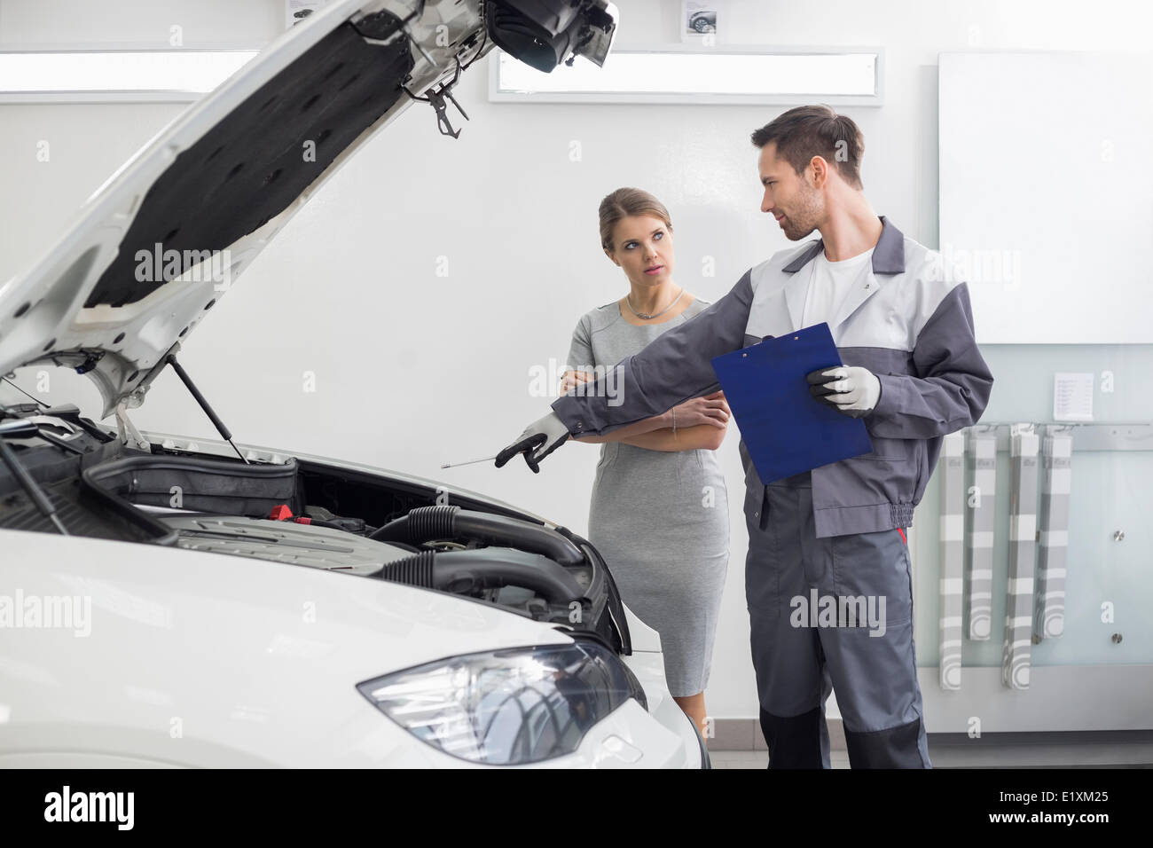 Young male repairman explaining car engine to female customer in ...