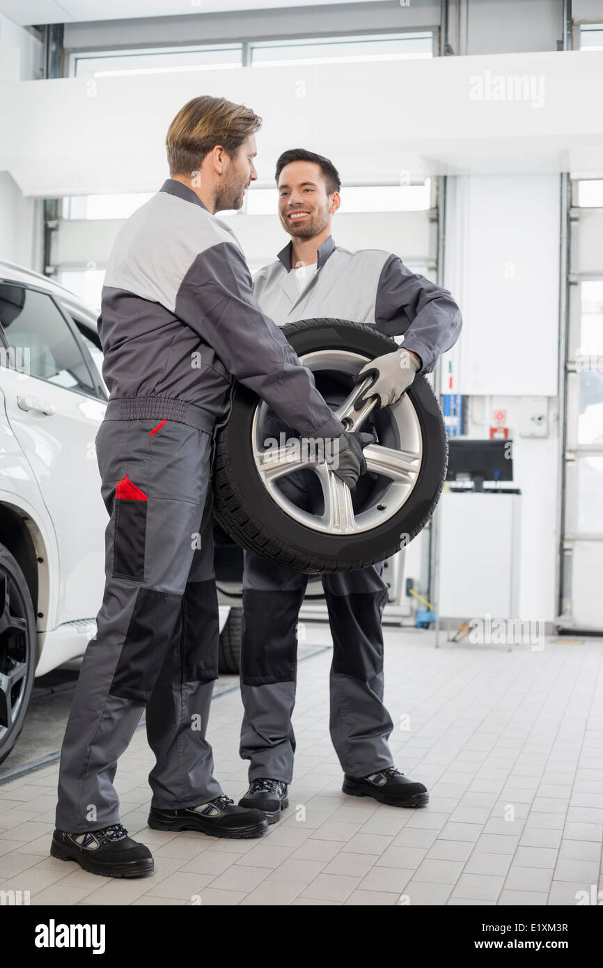 Full length of maintenance engineers carrying tire in car workshop ...