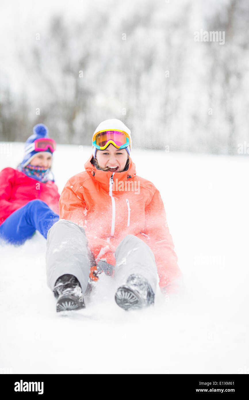 Young woman enjoying sled ride in snow with friend in background Stock ...