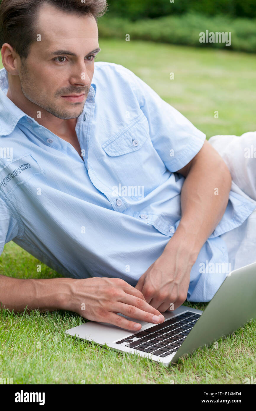 Thoughtful young man with laptop in park Stock Photo - Alamy