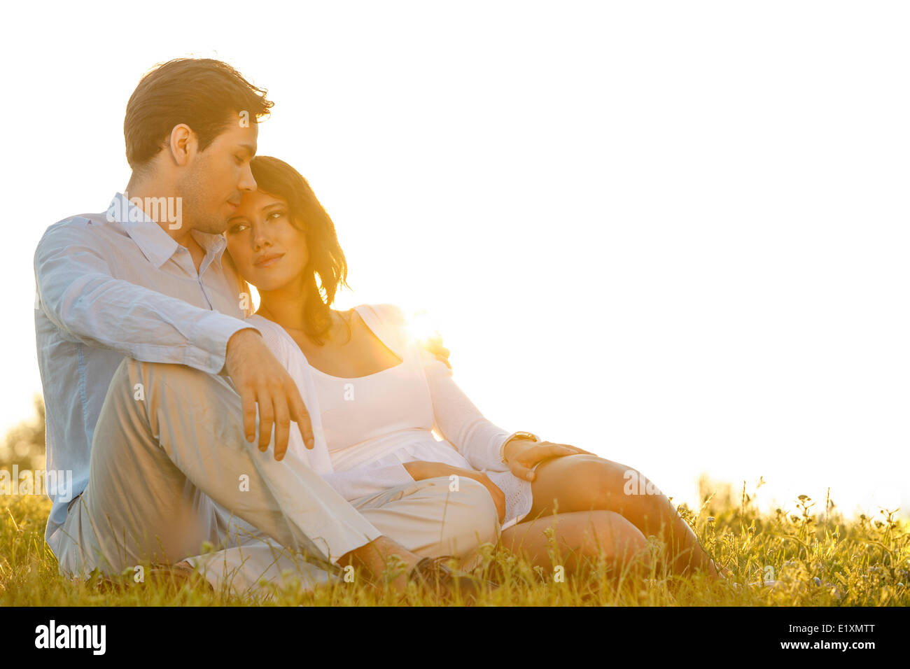Loving young couple sitting on grass against clear sky Stock Photo - Alamy