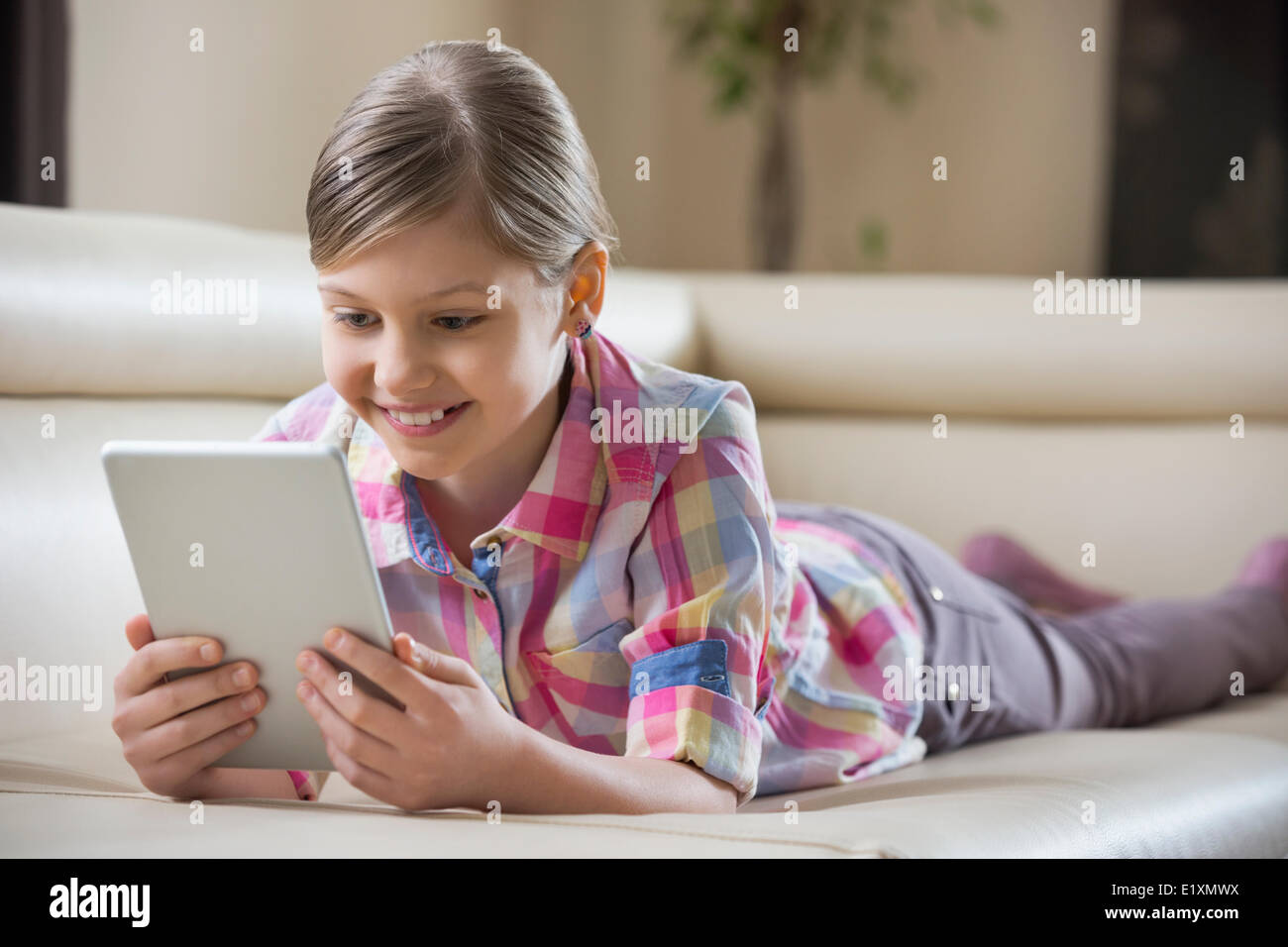 Smiling girl using tablet PC while lying on sofa at home Stock Photo ...