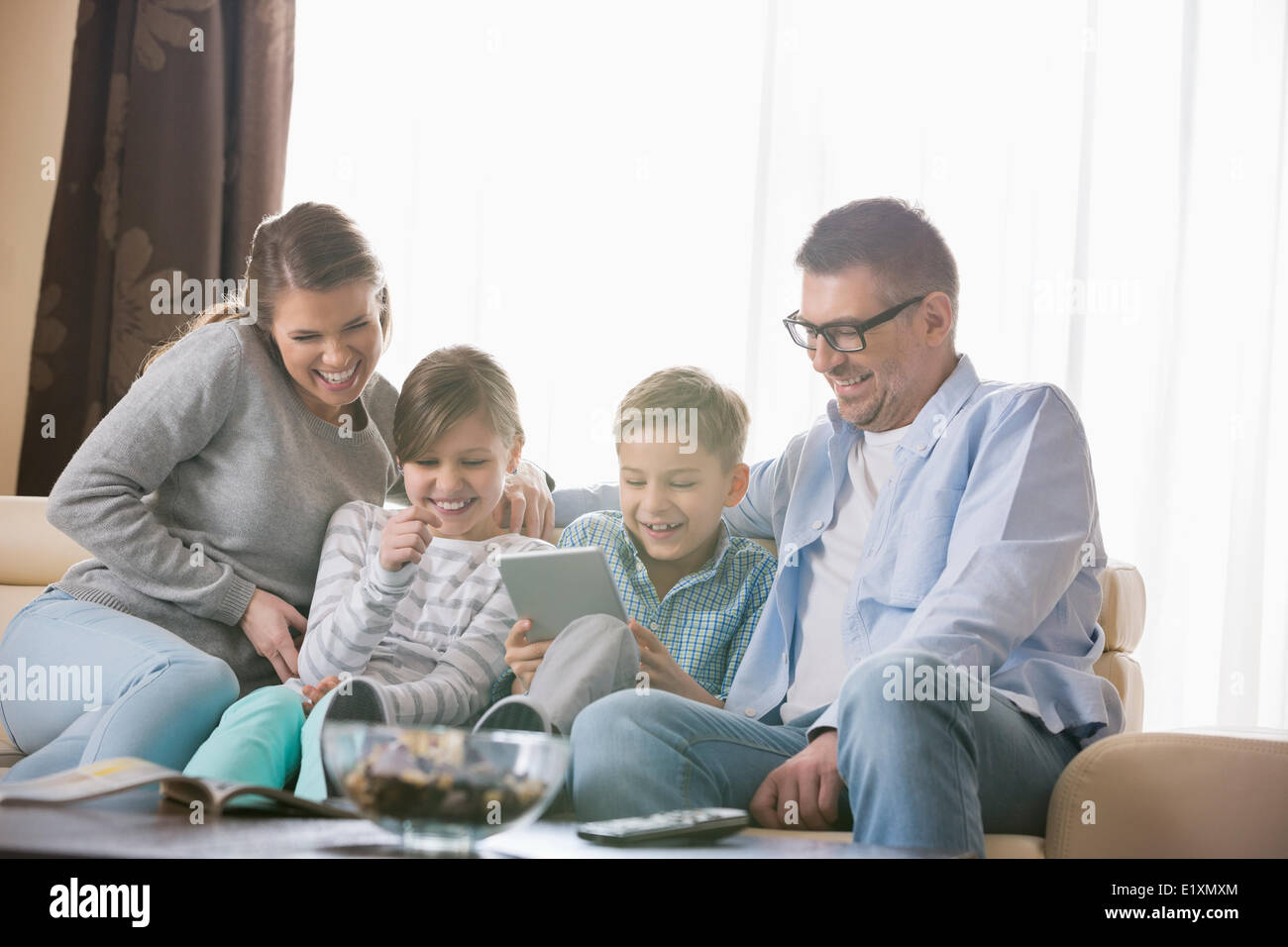 Cheerful family using tablet PC together in living room Stock Photo - Alamy