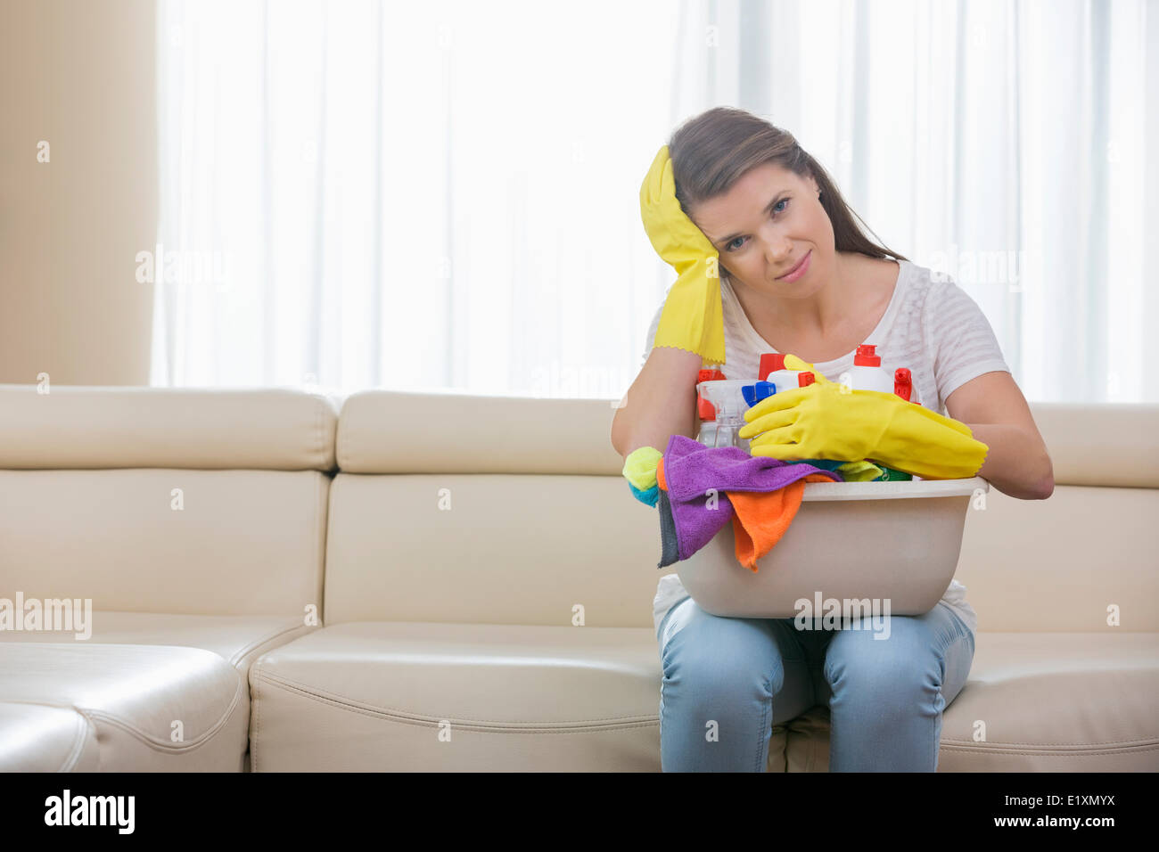 Portrait of tired woman with basket of cleaning supplies sitting on ...