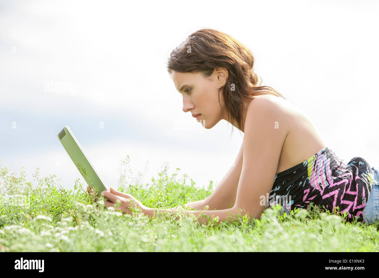 Side view of young woman using Tablet PC while lying on grass against ...