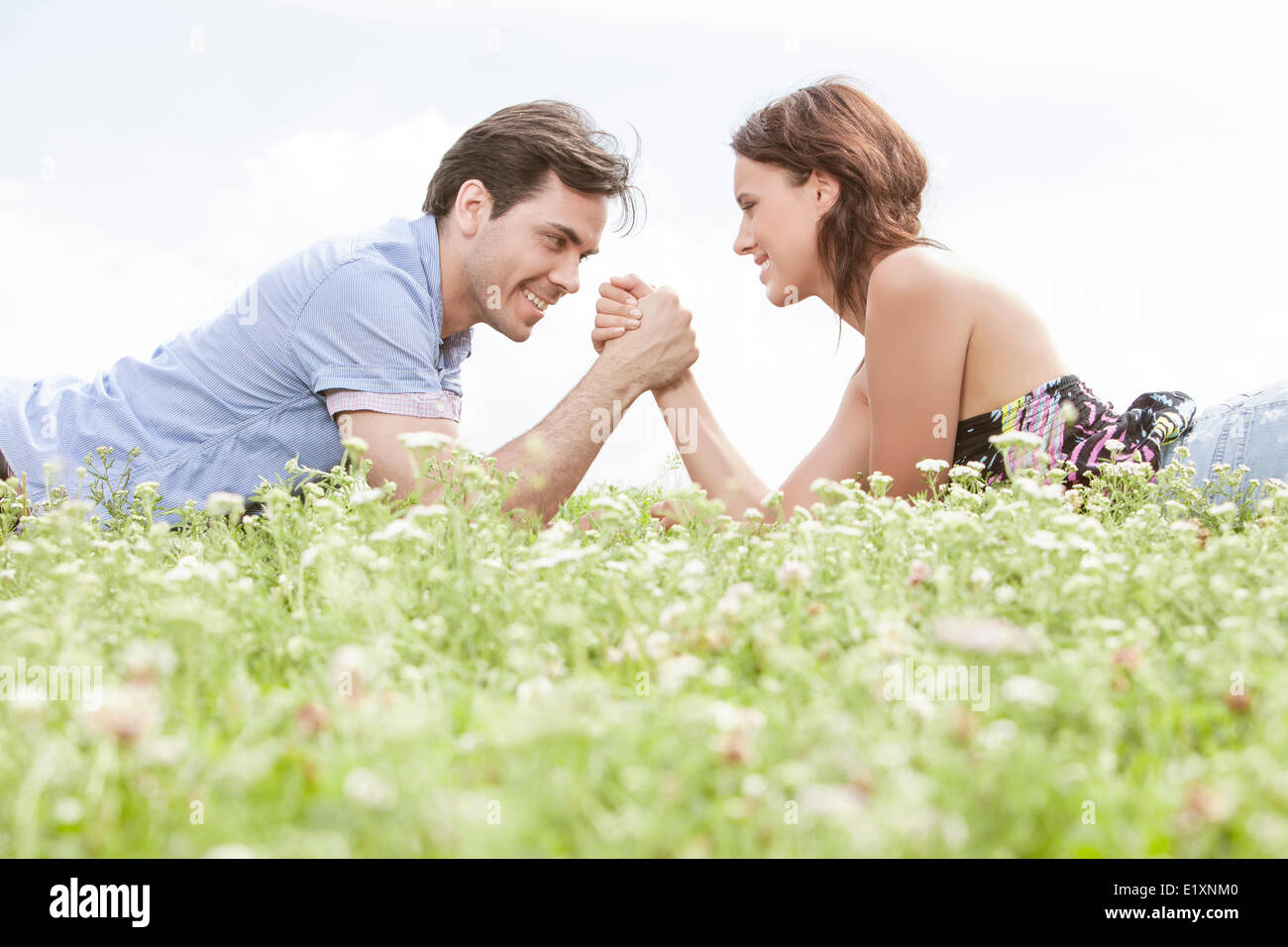 Side view of young couple arm wrestling while lying on grass against ...
