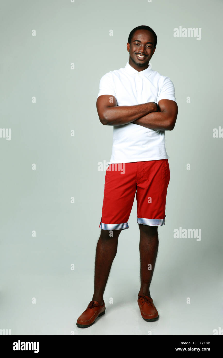 Full length portrait of a happy african man with arms folded on gray ...