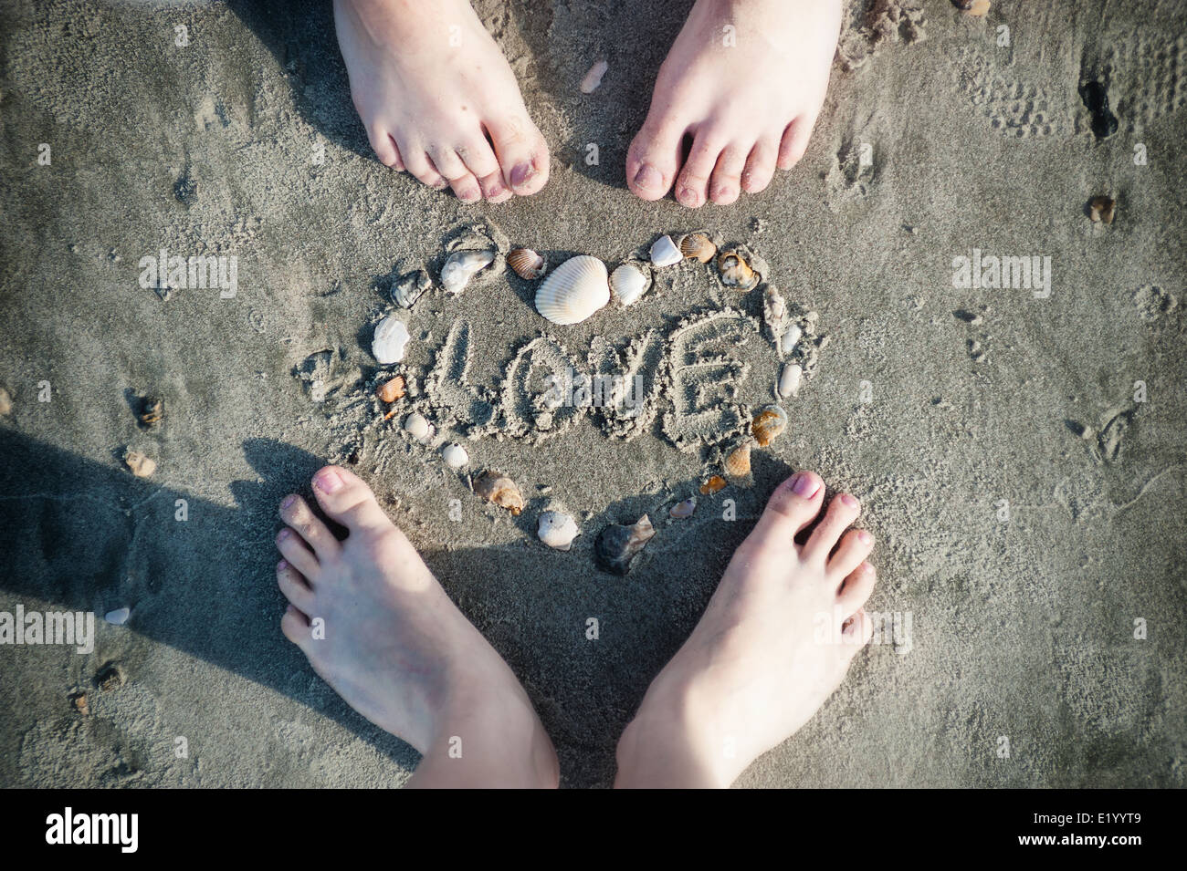 Feet of loving couple and a heart made of seashells on the sand on the ...