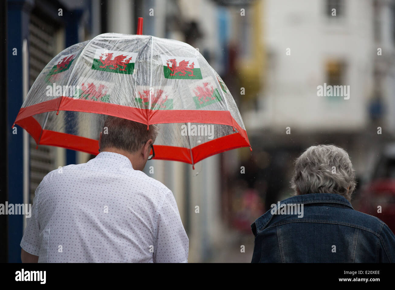A man with an umbrella decorated with Welsh flags walks on a street in ...